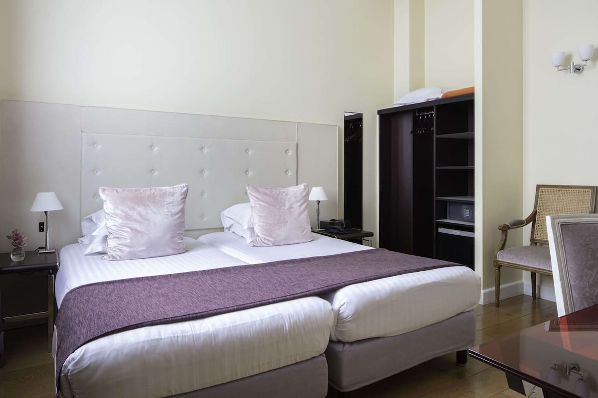 Quarto de hotel com uma cama grande, mesa de cabeceira, escrivaninha, cadeira e guarda-roupa.