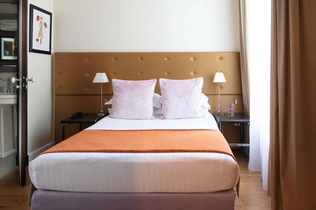 Quarto de hotel com uma cama grande, duas luminárias de cabeceira, uma mesinha de cabeceira e um quadro na parede.