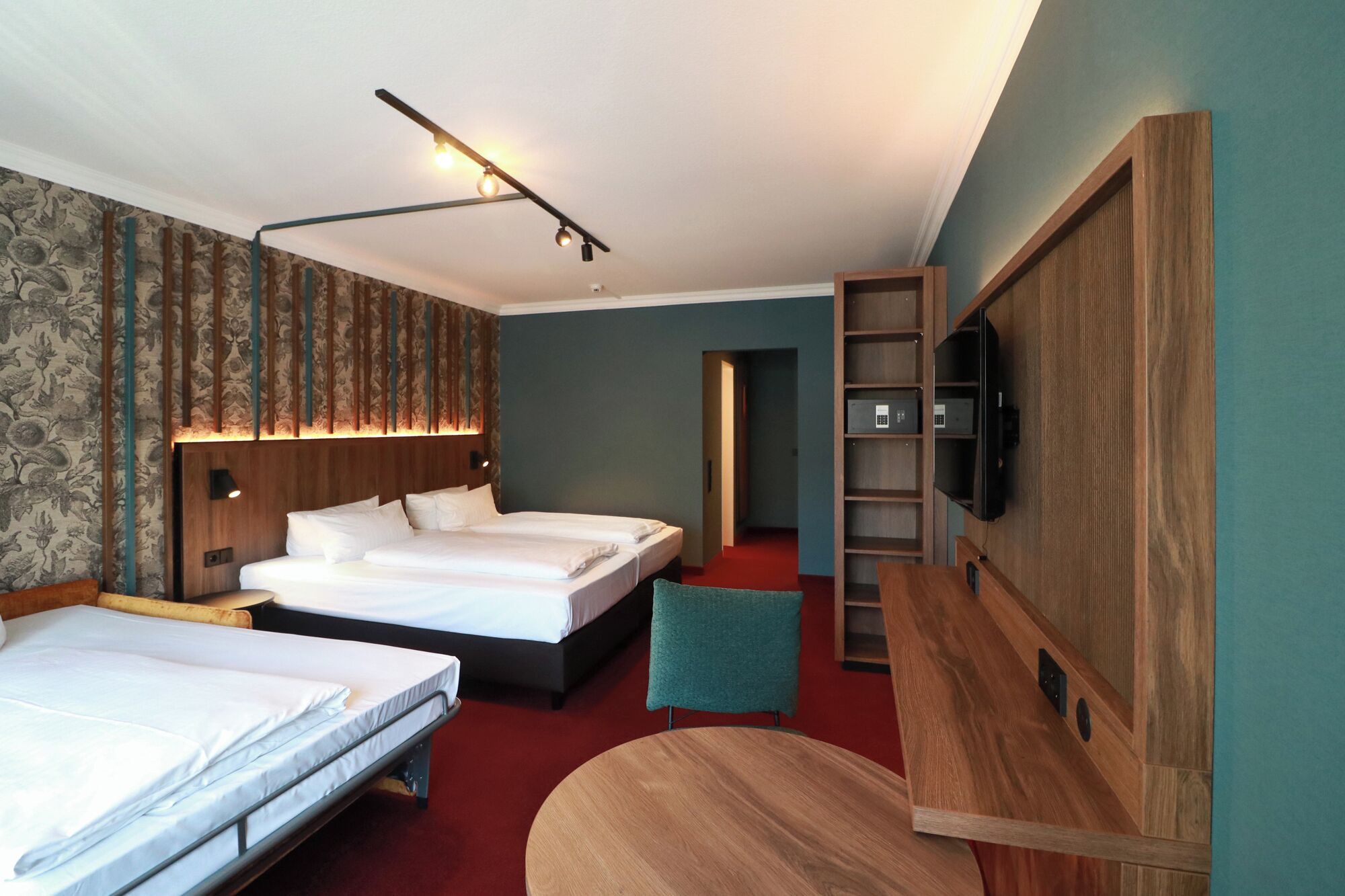 Quarto de hotel com duas camas, televisão, escrivaninha de madeira e tapete vermelho.