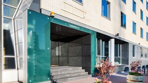 A modern building with a glass entrance, a sign reading "Launhardstr. 2-4", and a paved area with a planter.