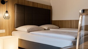 Quarto de hotel moderno com uma cama grande, uma mesa de cabeceira com abajur e um painel de parede de madeira.