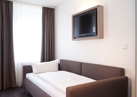 Quarto de hotel moderno com uma cama de solteiro, televisão de tela plana na parede e uma janela com cortinas.
