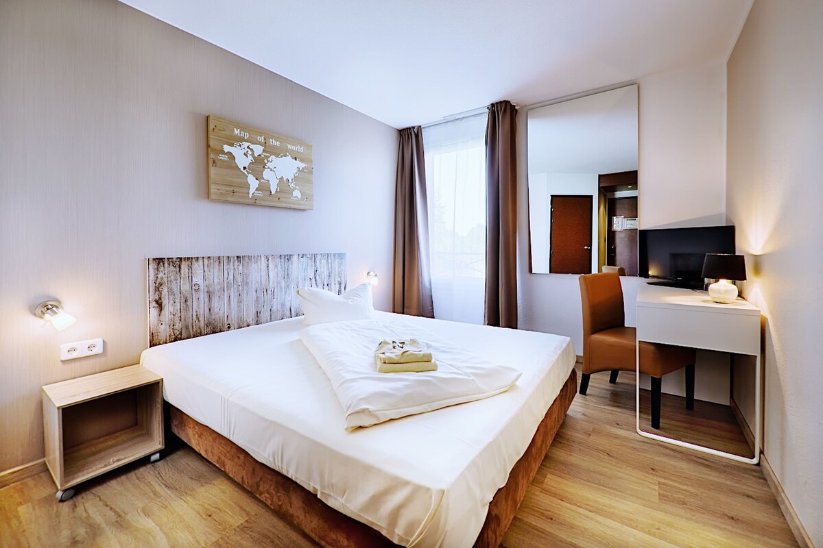 Quarto de hotel com uma cama grande, uma mesa, uma cadeira, um mapa na parede e uma TV.