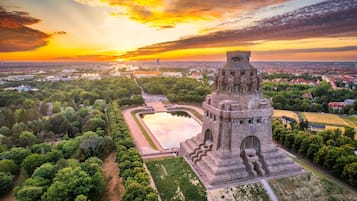 Um grande monumento de pedra com estátuas, rodeado por um parque com um lago espelhado, ao pôr do sol.
