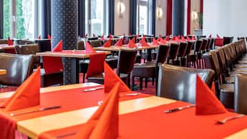 Um restaurante com várias mesas dispostas em fileiras, cada uma com guardanapos e talheres vermelhos.