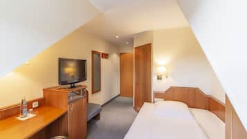 Quarto de hotel com cama, escrivaninha com televisão, espelho e porta.