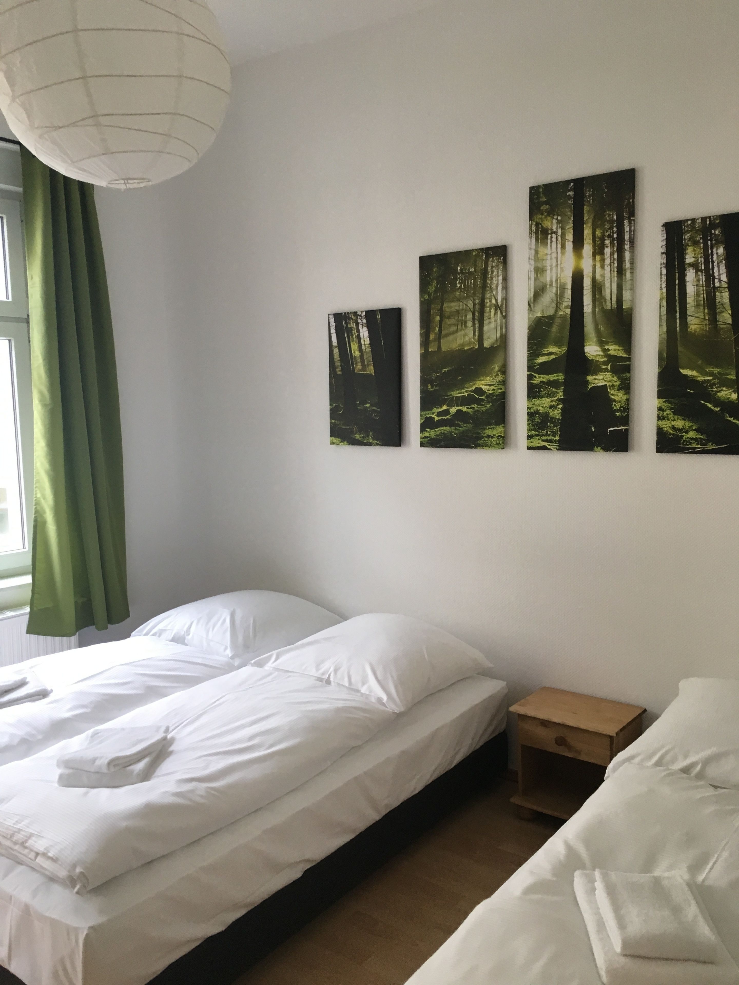 Quarto com duas camas, uma mesa de cabeceira e três quadros com tema de floresta.
