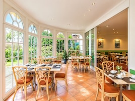 Restaurante com grandes janelas, cadeiras de vime e chão de azulejos.