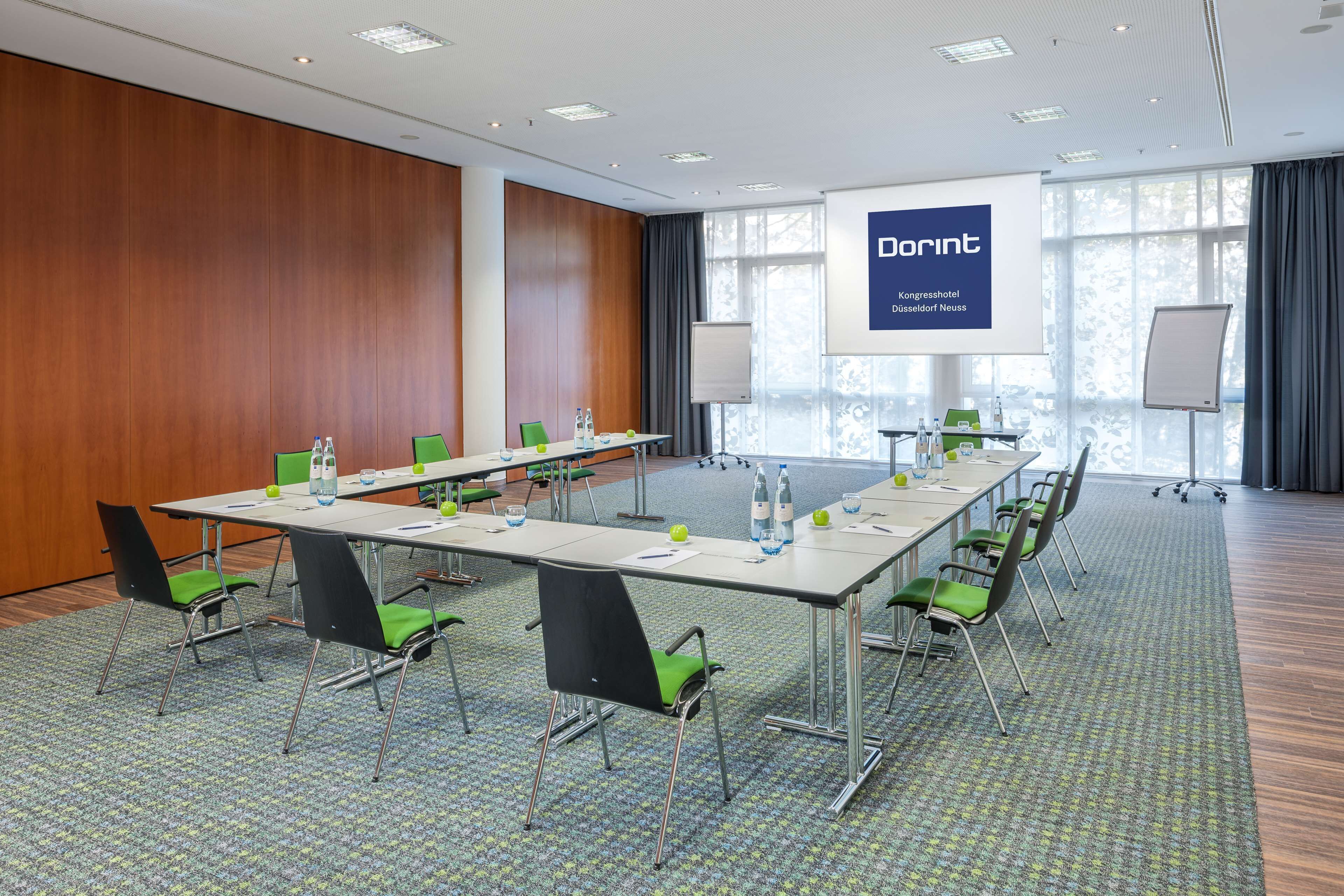 Uma sala de conferências com uma mesa comprida, cadeiras verdes e uma tela de projeção exibindo 'Dorint'.