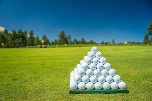 Uma pirâmide de bolas de golfe sobre um tapete verde num campo de golfe.