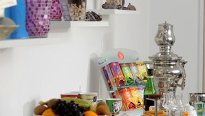 Uma mesa de buffet com diversos alimentos, incluindo uma tigela de frutas, lanches embalados e uma máquina de café.