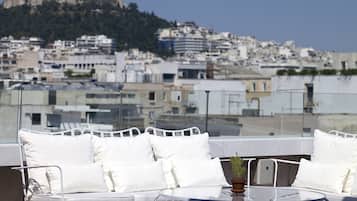 Terraço no telhado com mobiliário branco para área externa, uma mesa de vidro e um vaso com planta.