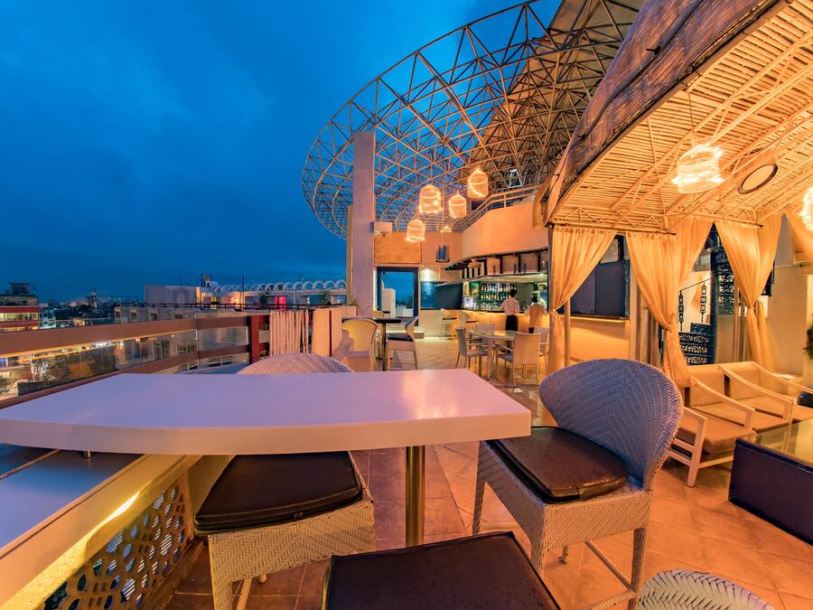 Uma área externa com assentos de vime, um bar e vista para o horizonte da cidade.