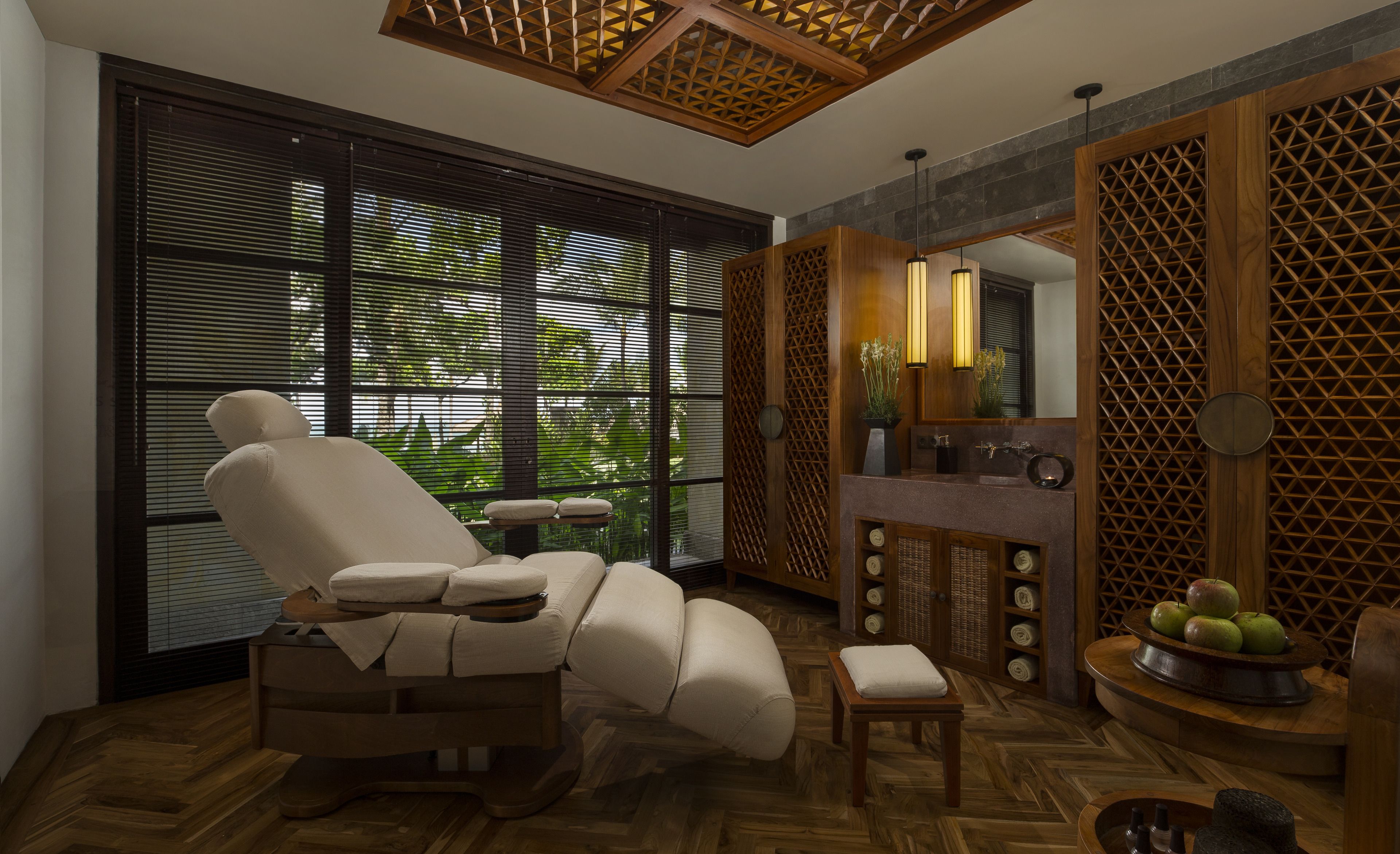Um quarto de spa com uma cadeira de massagem, uma mesinha, uma pia e um armário de madeira com toalhas.