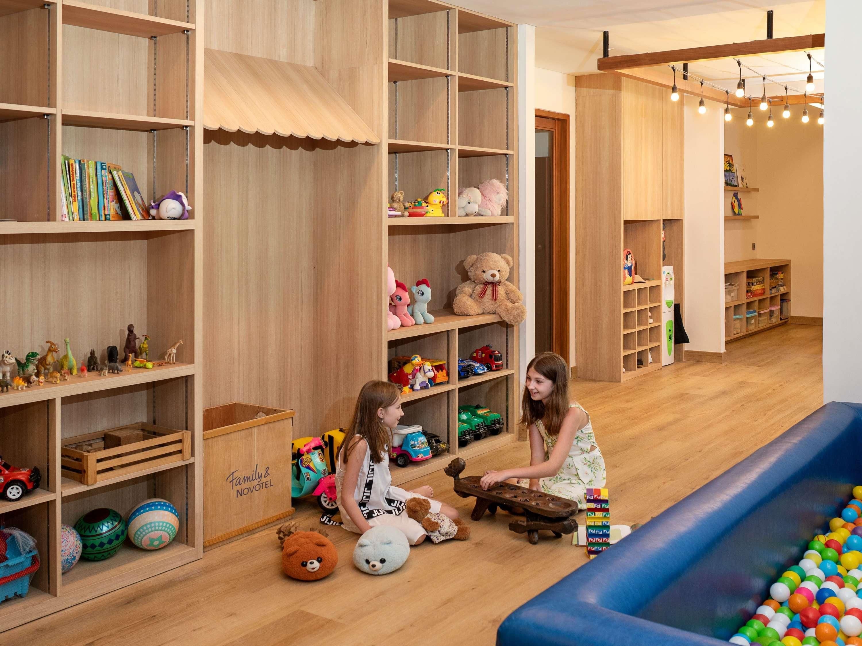 Espaço de recreação infantil com prateleiras de madeira, brinquedos e piscina de bolinhas.
