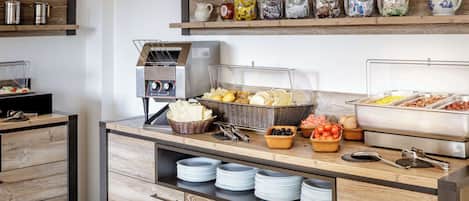 Disposição de buffet com diversos alimentos, uma máquina de café e potes decorativos nas prateleiras.