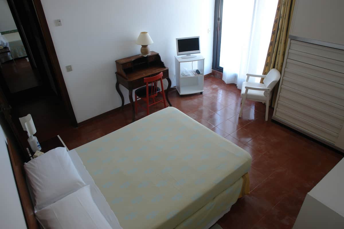 Quarto com cama, escrivaninha com computador, cadeira e televisão.