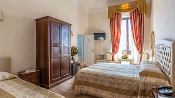 Quarto de hotel com duas camas, um guarda-roupa, uma televisão, uma mesa com telefone e uma janela com cortinas.