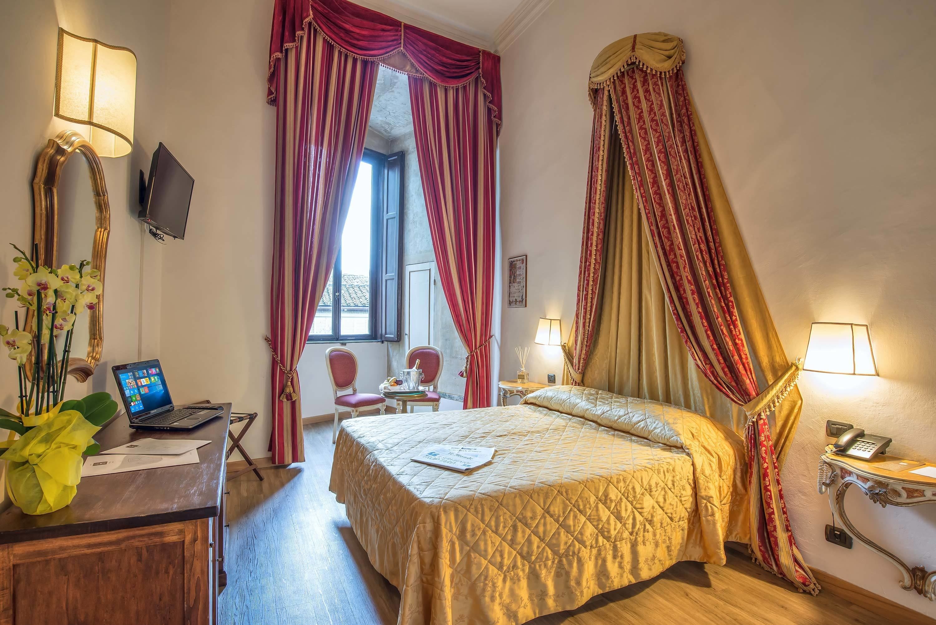 Quarto de hotel com cama, escrivaninha, laptop, cadeira e cortinas.