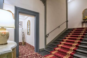 Escada com degraus revestidos de carpete vermelho e corrimão, conduzindo a um andar superior.