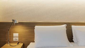 Cama bem arrumada com almofadas brancas, abajur e cabeceira de madeira.