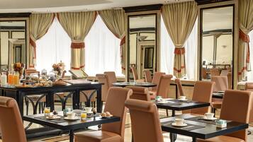 Espaço de refeições de hotel com várias mesas e cadeiras, buffet de café da manhã e amplas janelas com cortinas.