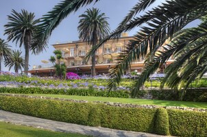 Hotel com jardim, palmeiras e um prédio com varandas.