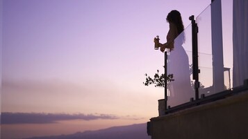 Uma pessoa está na varanda com uma câmera, admirando a paisagem urbana ao pôr do sol.