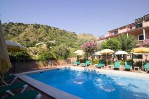 Um hotel com piscina, área de estar externa e paisagem campestre ao fundo.