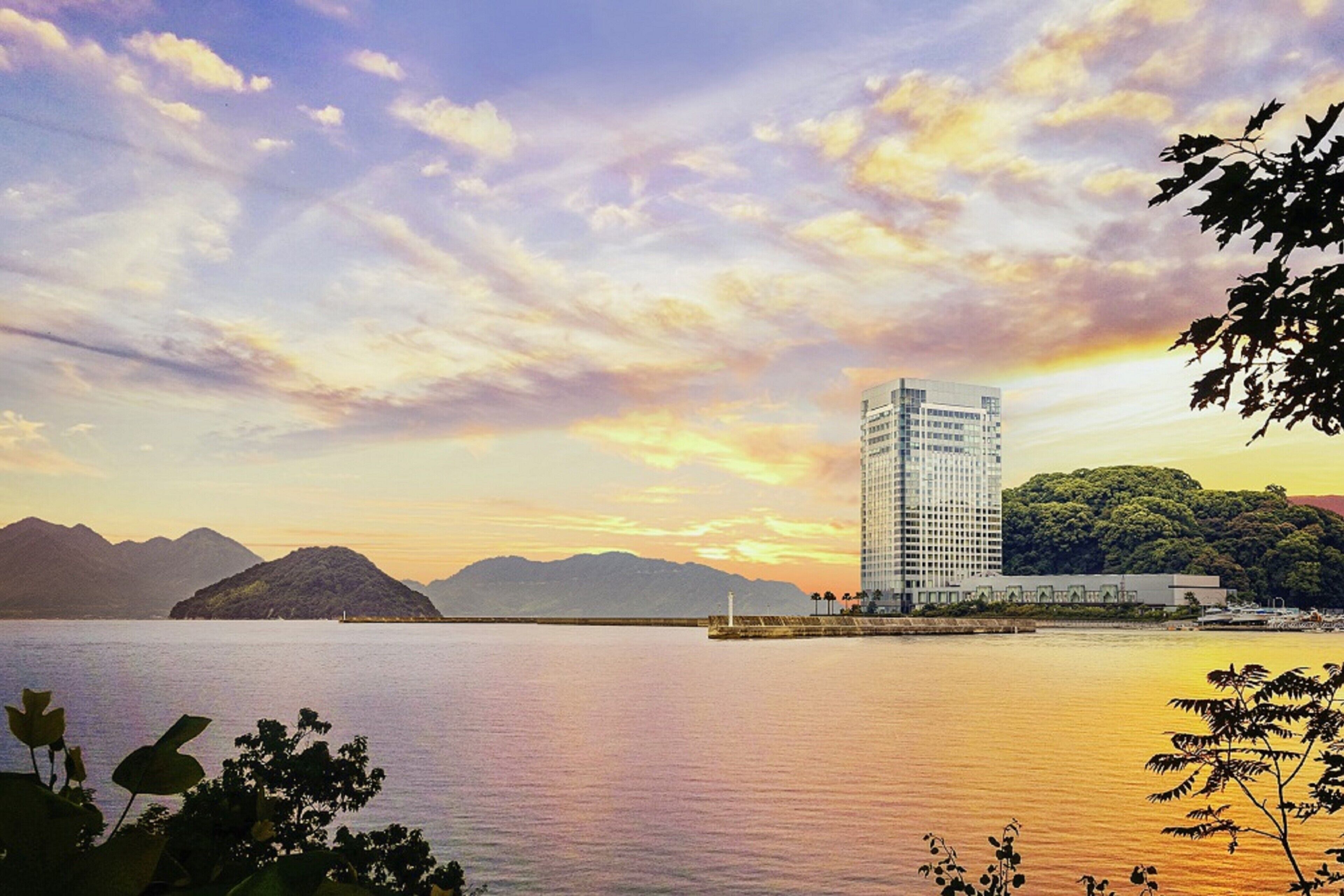 Um hotel alto com vista para um lago calmo e montanhas ao fundo.
