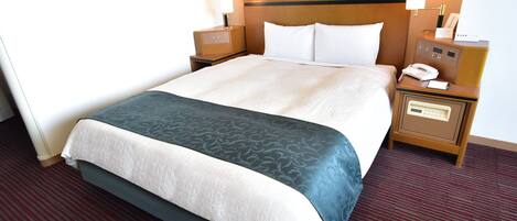 Quarto de hotel com cama, duas mesinhas de cabeceira, um criado-mudo, luminária, telefone e termostato.