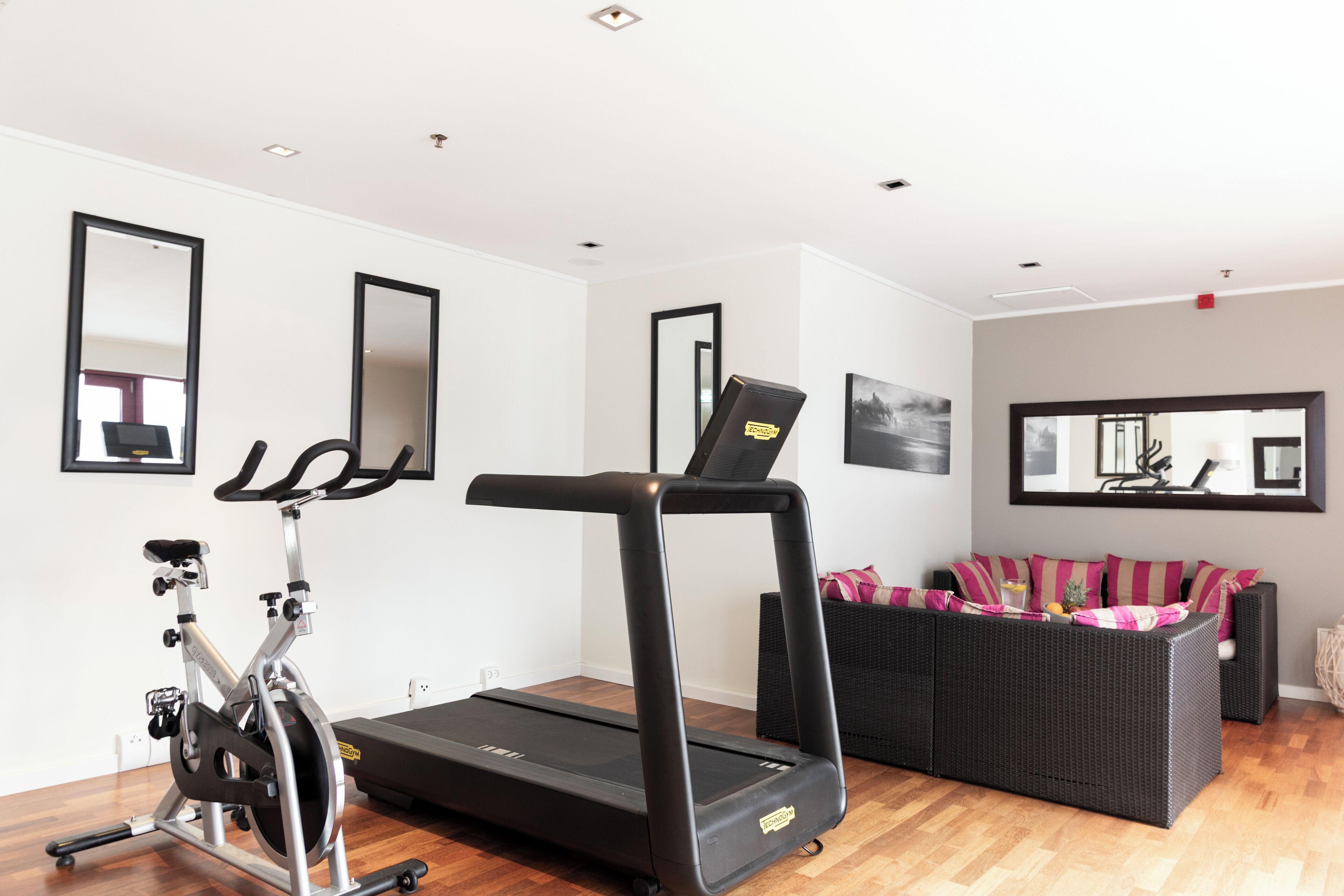 Uma sala de estar moderna com uma bicicleta ergométrica, um sofá e um espelho grande.