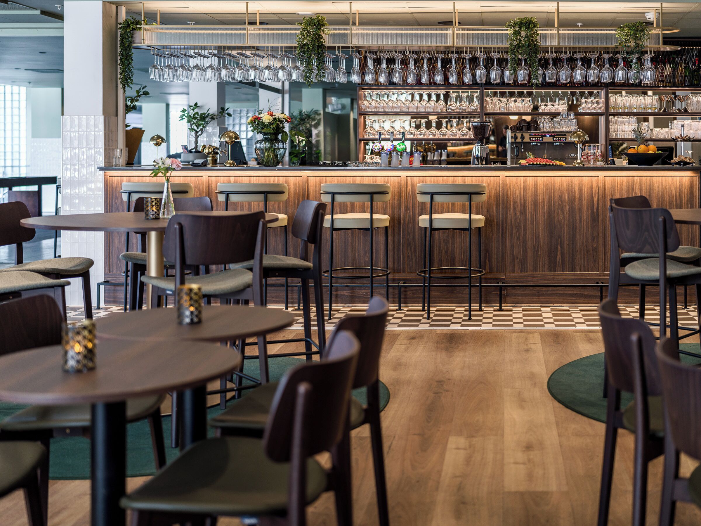 Uma área de bar com vários bancos, um balcão com diversos copos e um padrão de piso xadrez.