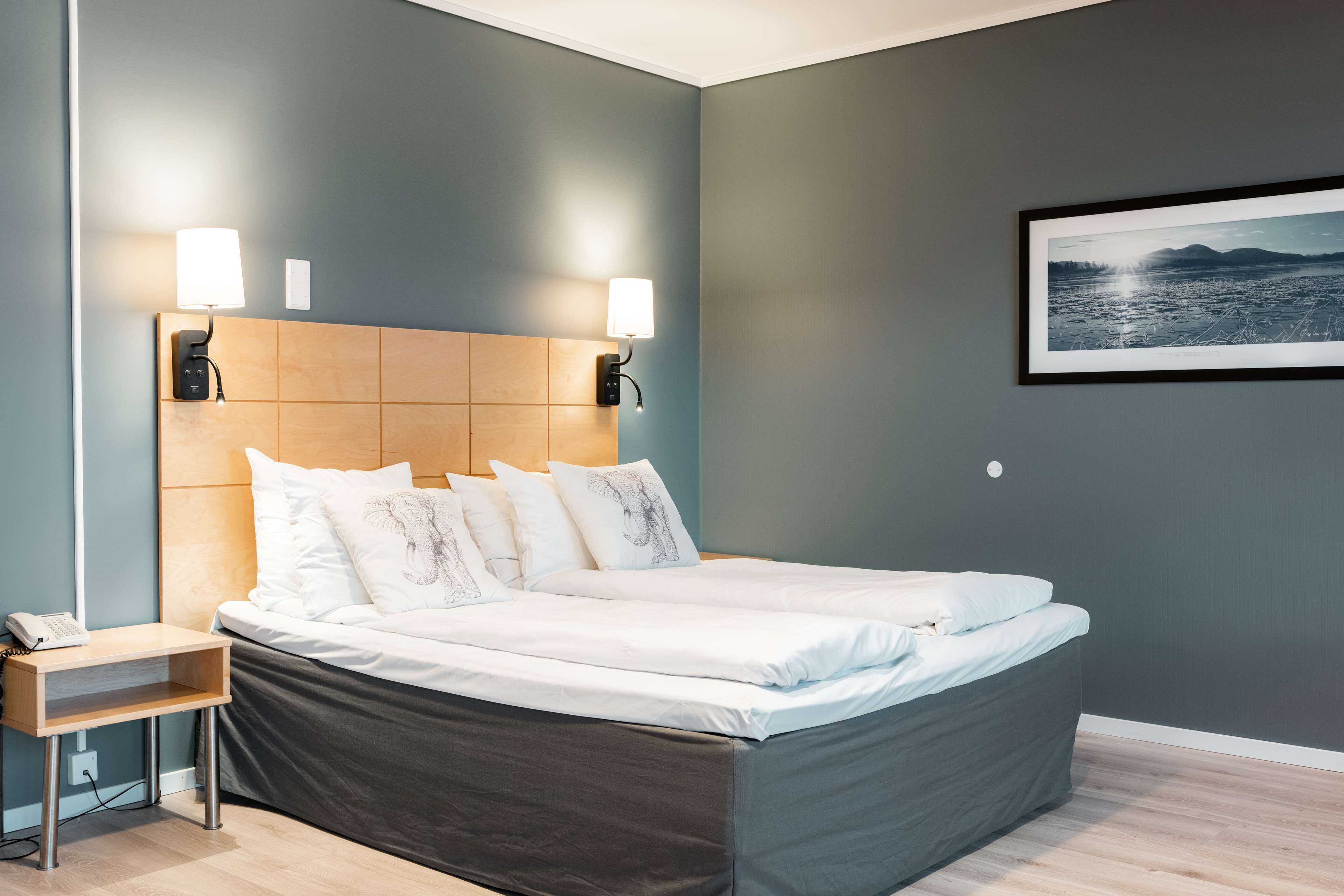 Quarto moderno com cabeceira de madeira, mesa de cabeceira com abajur e quadro na parede.