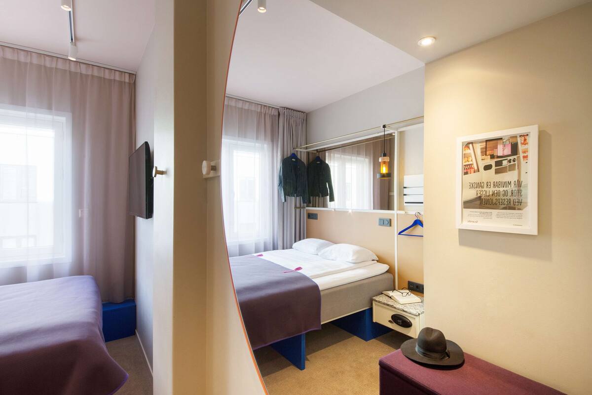 Quarto de hotel com duas camas, uma mesinha de cabeceira, um espelho e um quadro na parede.