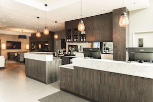 Uma área de bar moderna com balcão de madeira, iluminação pendente e um ponto de bar com monitor de computador.