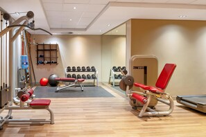Uma academia com diversos equipamentos de ginástica, incluindo um banco de musculação, halteres e uma esteira.