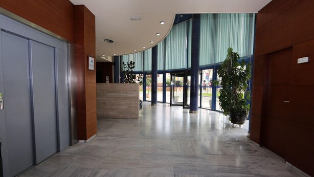Um hall amplo com piso de mármore, um balcão de recepção e grandes janelas com cortinas.