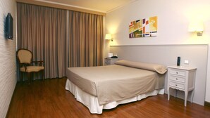 Quarto de hotel com cama, uma cadeira, mesa de cabeceira, luminária e uma obra de arte na parede.