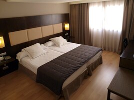 Quarto de hotel com cama grande, mesa de cabeceira com abajur e uma escrivaninha.