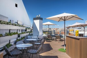 Terraço no telhado com área de estar ao ar livre, guarda-sóis e vista para a cidade.