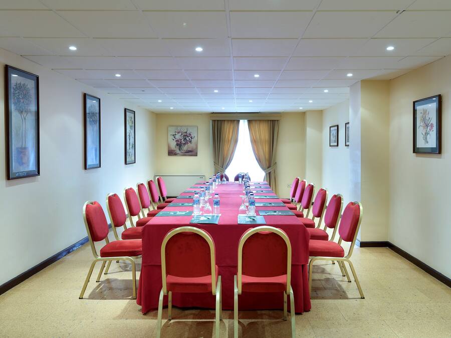 Uma sala de conferências com uma mesa comprida, cadeiras vermelhas e quadros nas paredes.