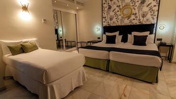 Quarto de hotel com uma cama grande, uma cama menor, um espelho e parede com desenho floral.