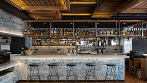 Uma área de bar com teto de madeira, balcão com banquetas e prateleiras cheias de garrafas.