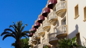 Um hotel com várias varandas, palmeiras e um céu azul límpido.