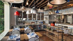 Interior de restaurante com mesas de madeira, cadeiras de metal e luminárias pendentes.