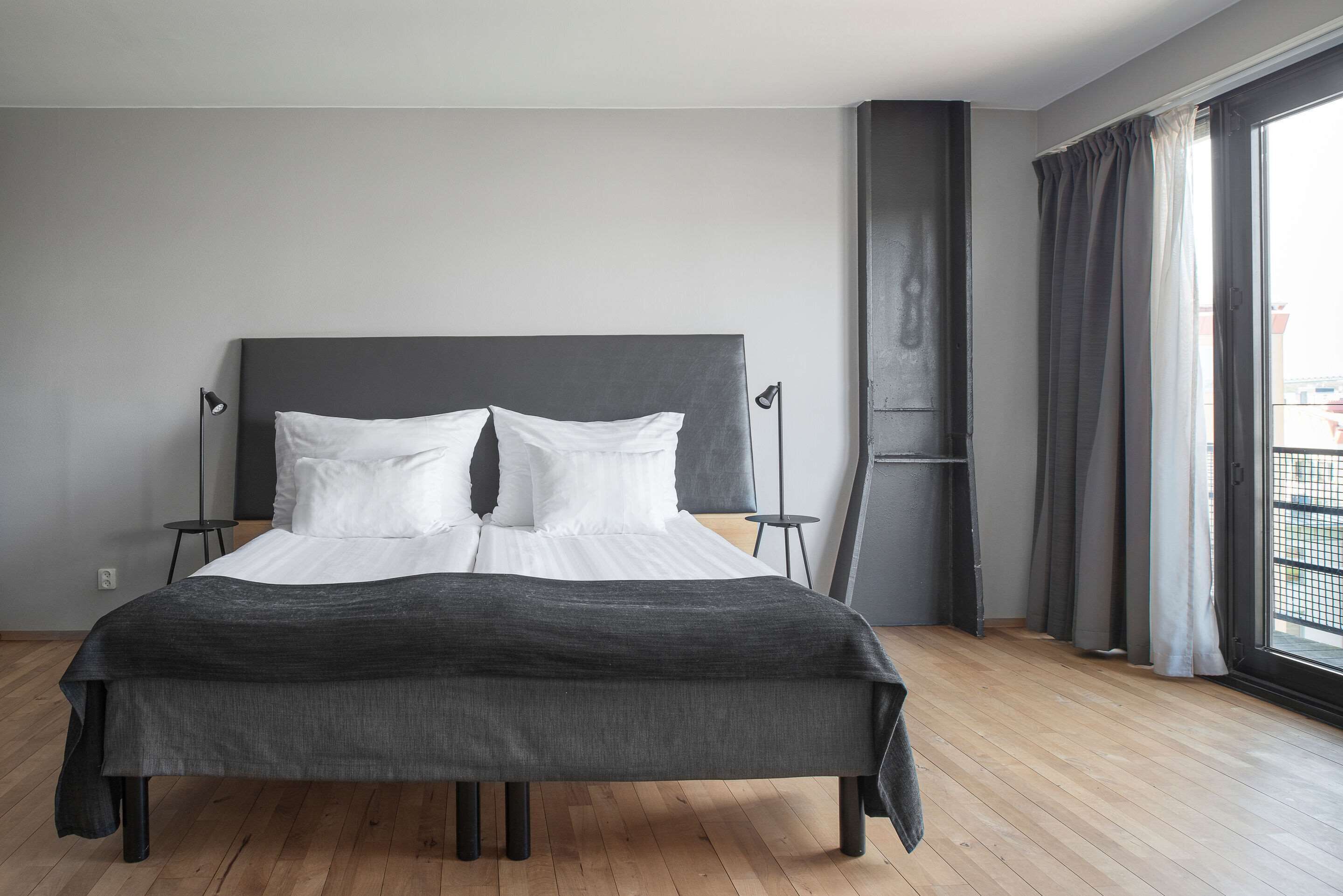 Quarto moderno com uma cama grande, duas mesas de cabeceira e vista para o exterior através de uma janela com cortinas.