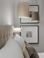 Quarto bem arrumado com uma cama, duas luminárias na parede e quadros emoldurados.