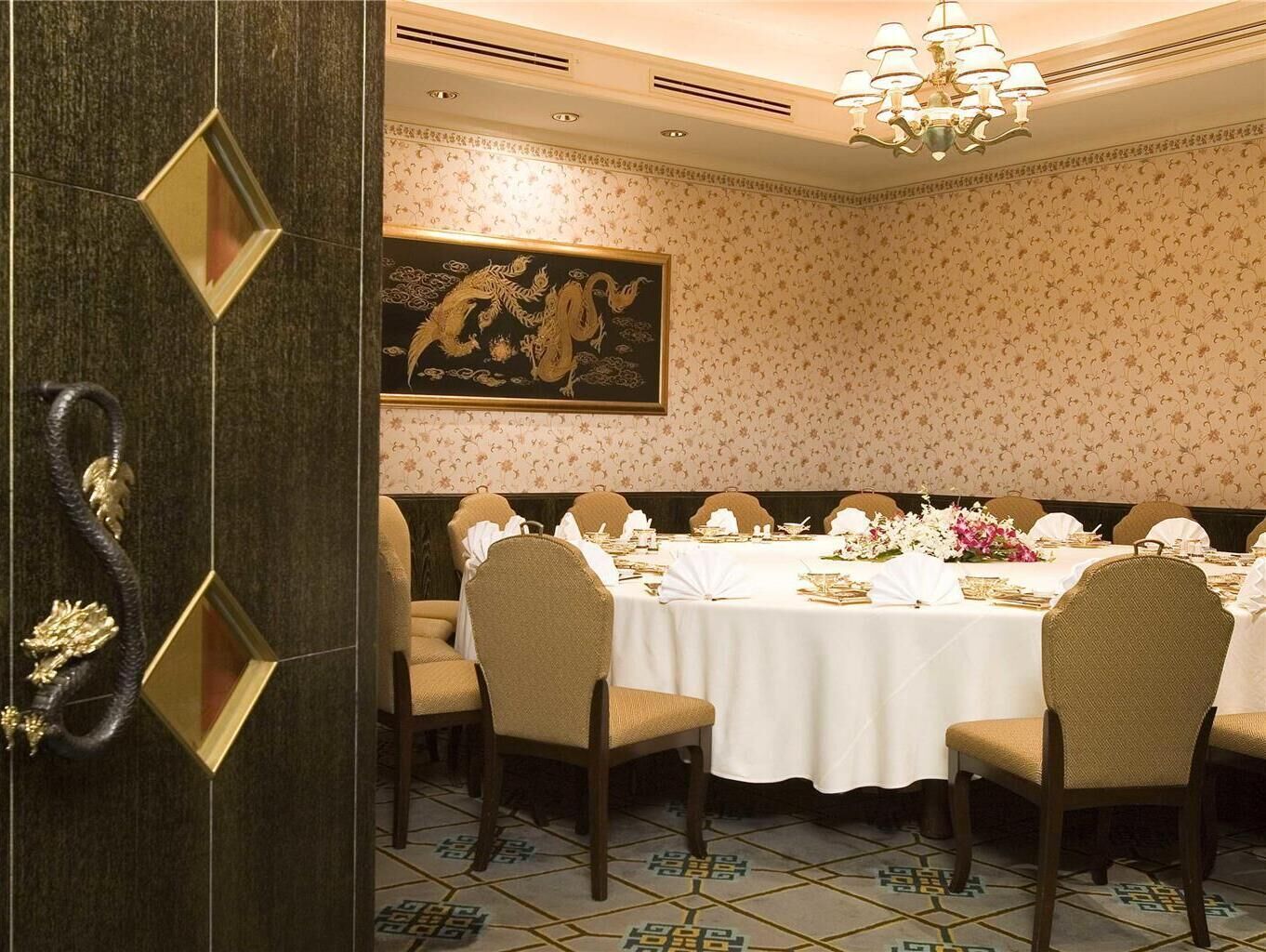 Uma sala de jantar formal com uma mesa redonda posta para refeição, cadeiras com capas brancas e um lustre.