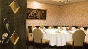 Uma sala de jantar formal com uma mesa redonda posta para refeição, cadeiras com capas brancas e um lustre.